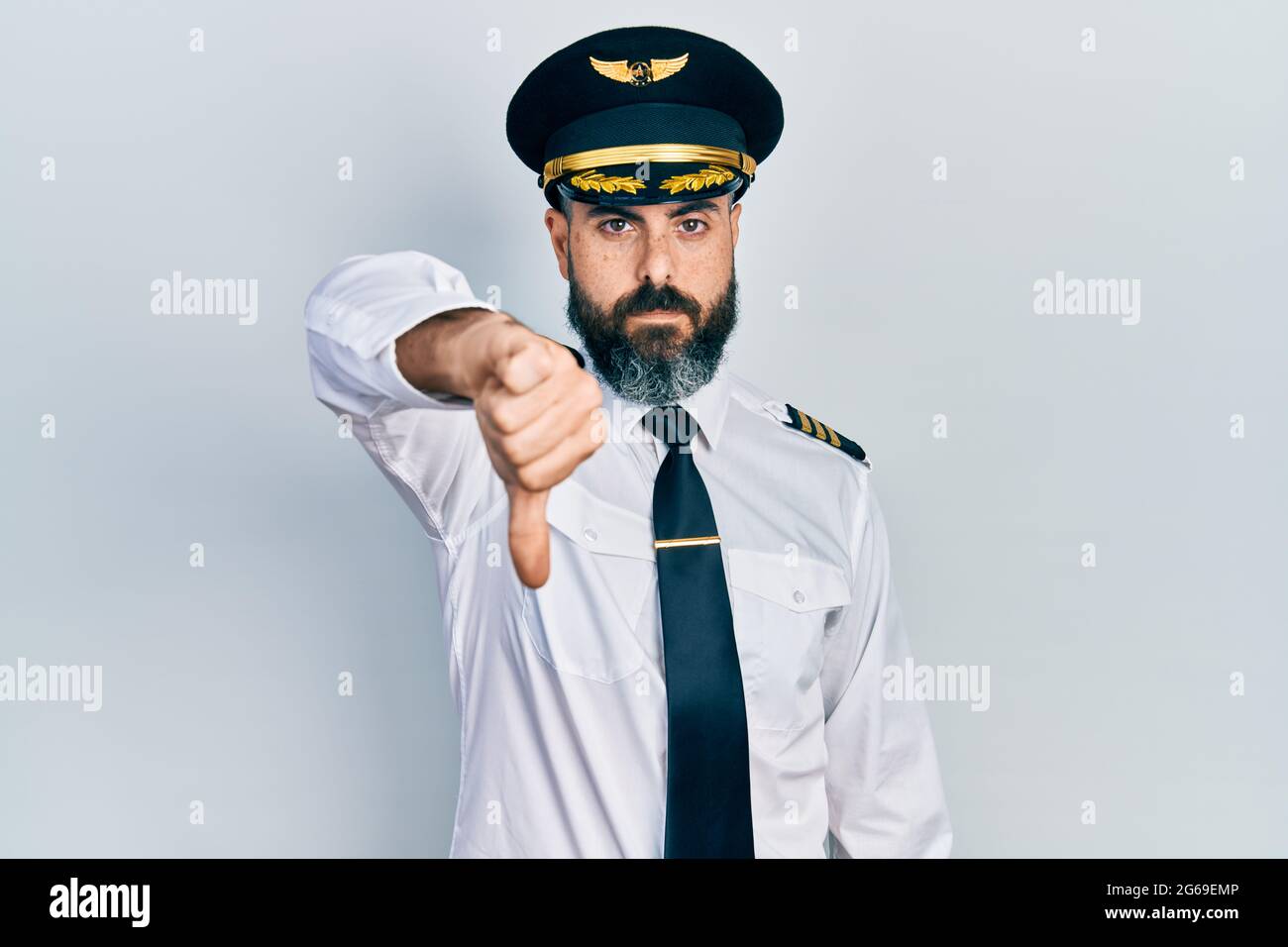 Young hispanic man wearing airplane pilot uniform looking unhappy and ...