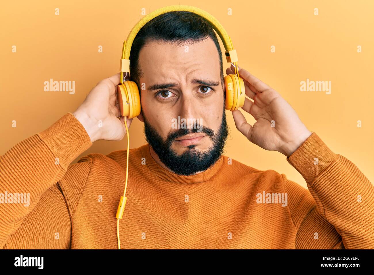 Young man with beard listening to music using headphones depressed and ...