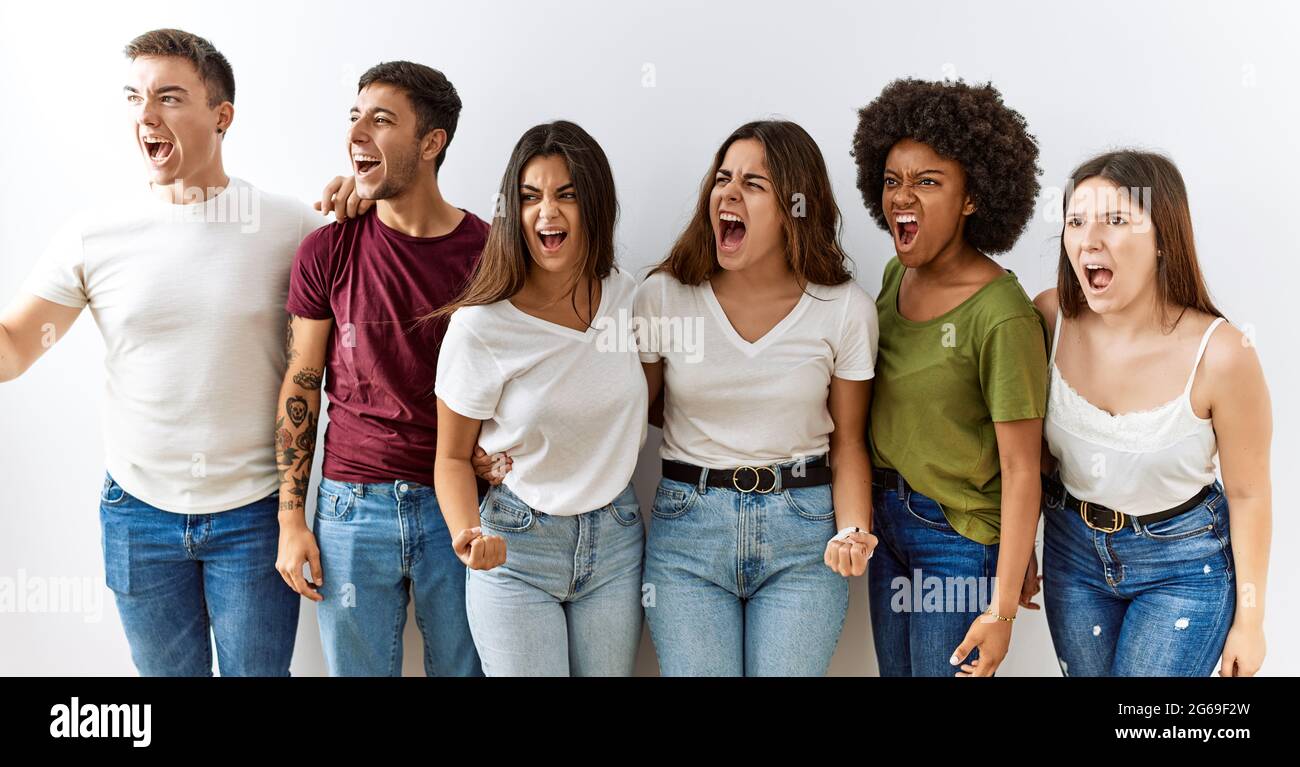 Group of young friends standing together over isolated background angry ...