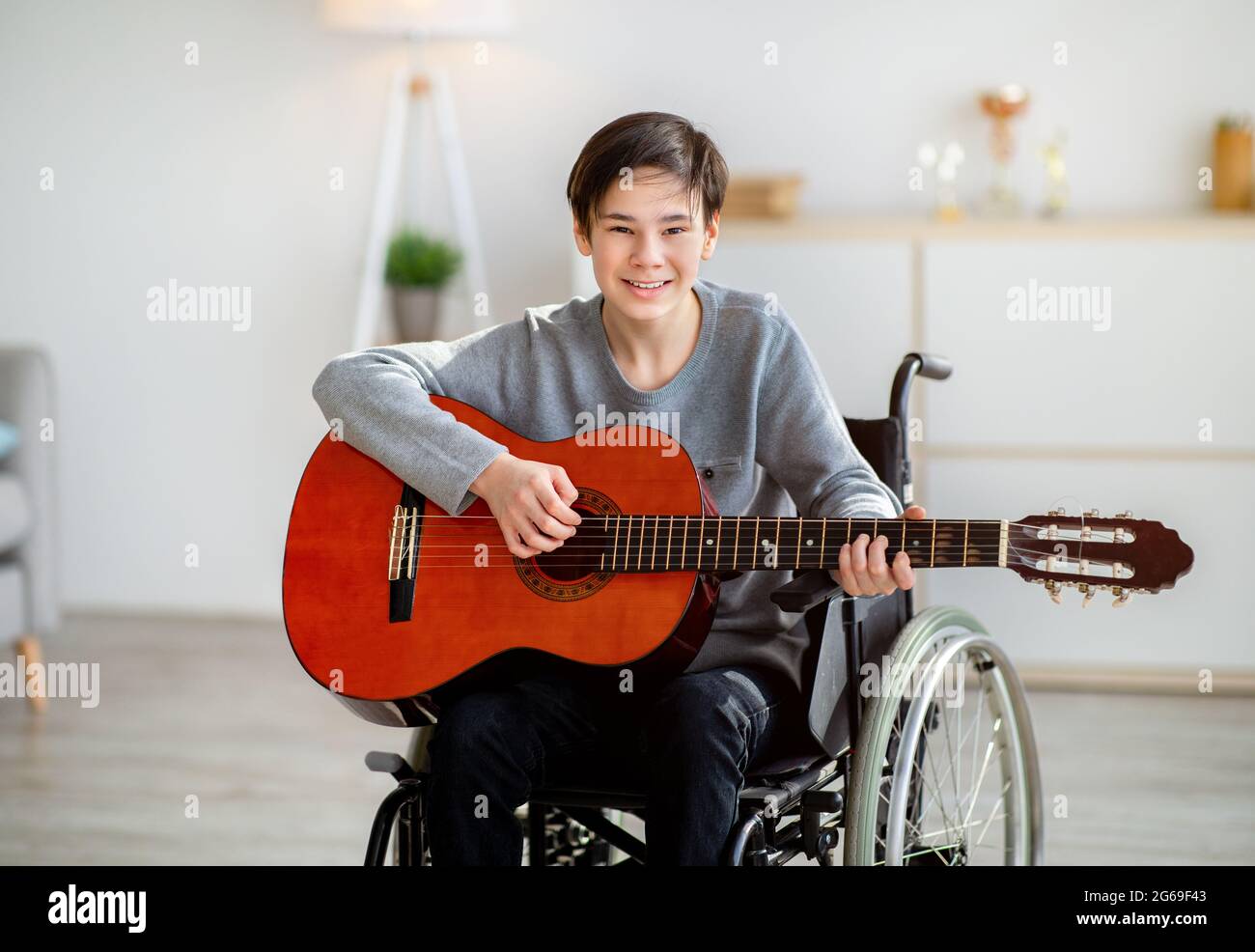 Happy disabled teen boy in wheelchair playing guitar, using musical ...