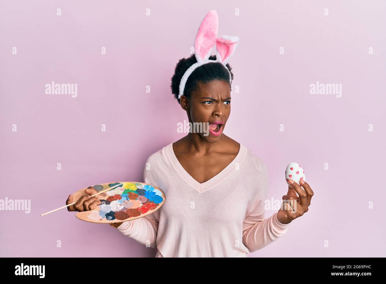 Young african american girl wearing cute easter bunny ears painting egg ...
