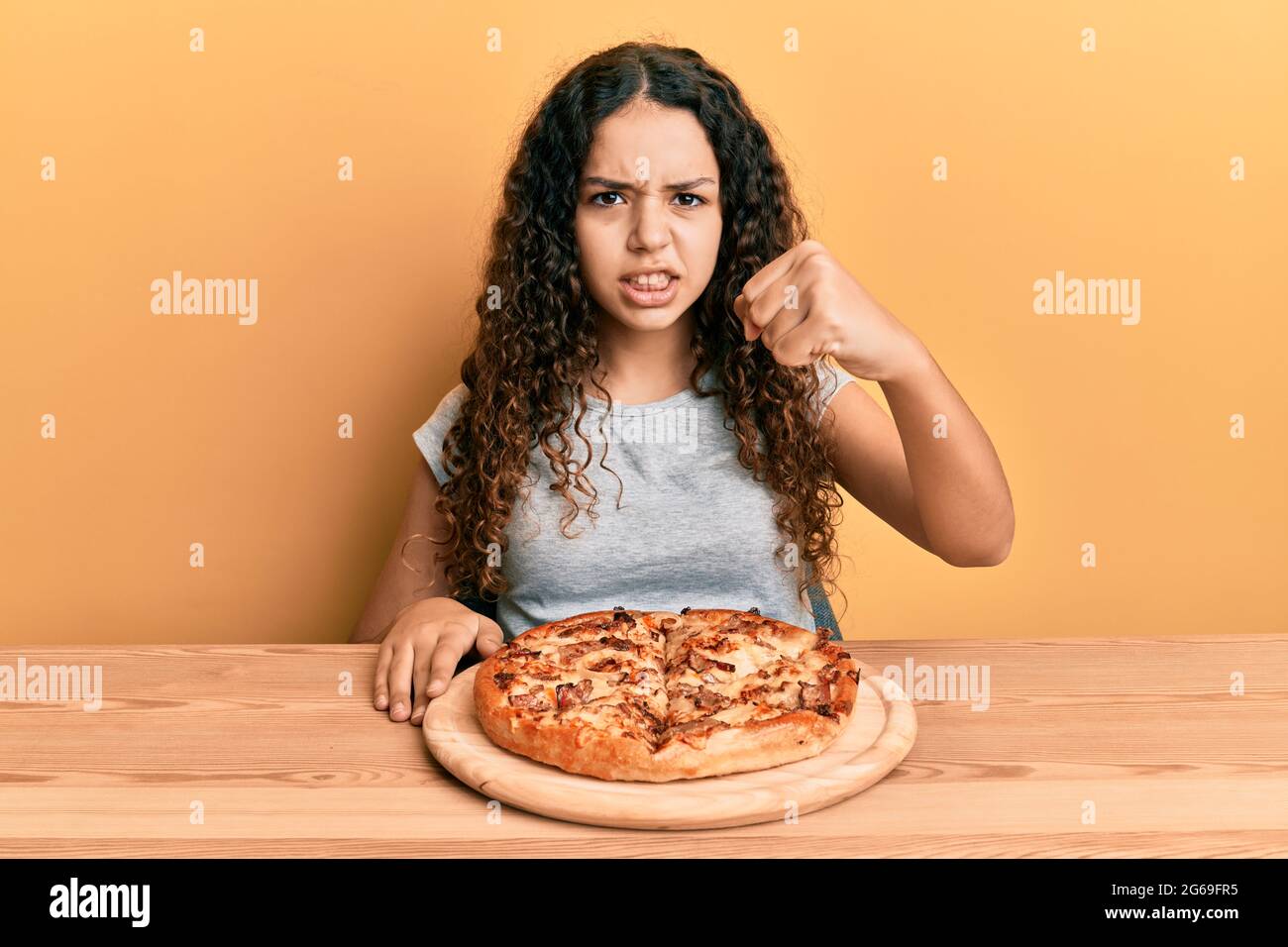Teenager hispanic girl eating italian pizza annoyed and frustrated ...