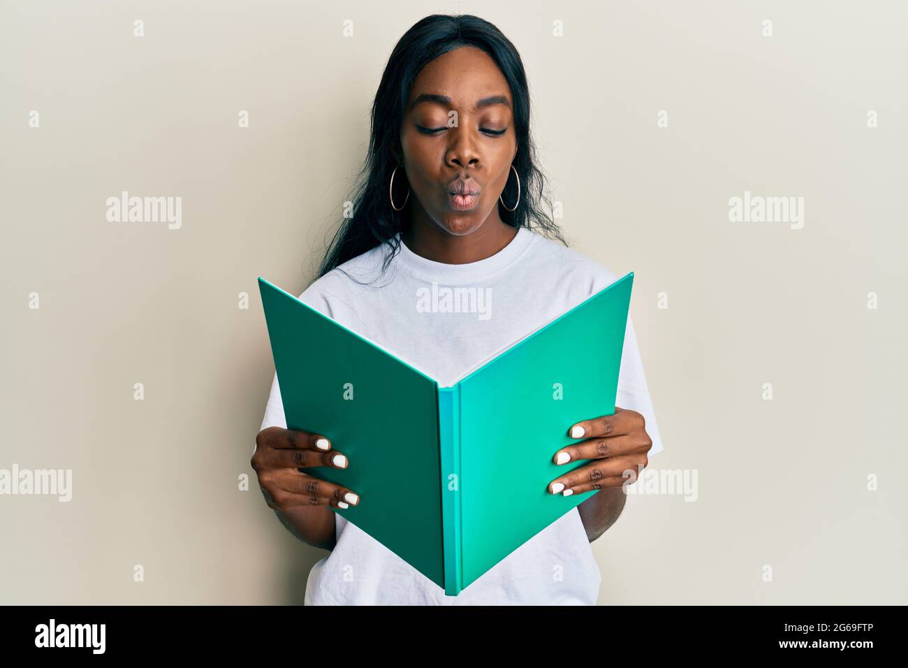 Young african american woman reading book making fish face with mouth ...