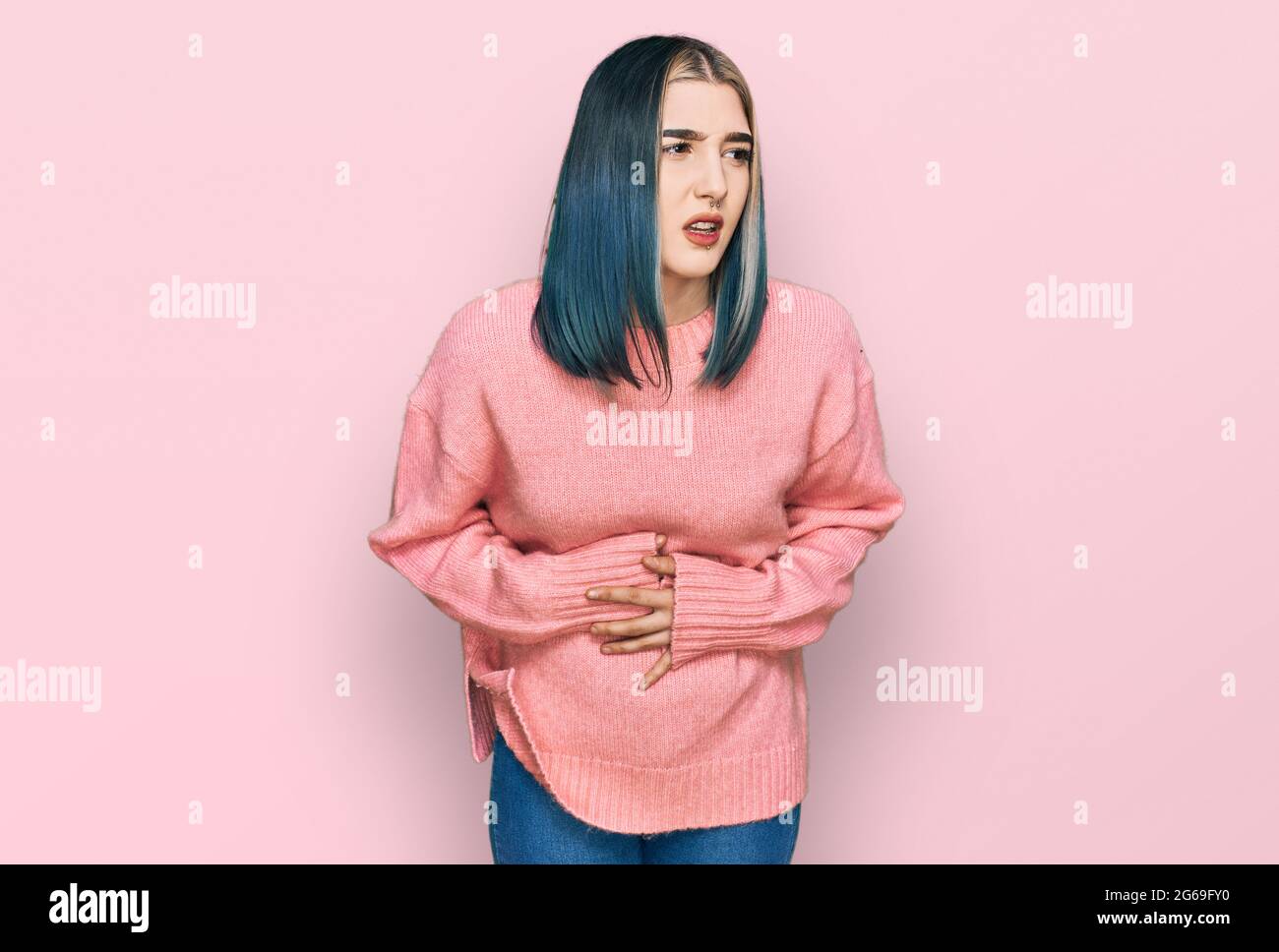 Young modern girl wearing pink wool winter sweater with hand on stomach ...