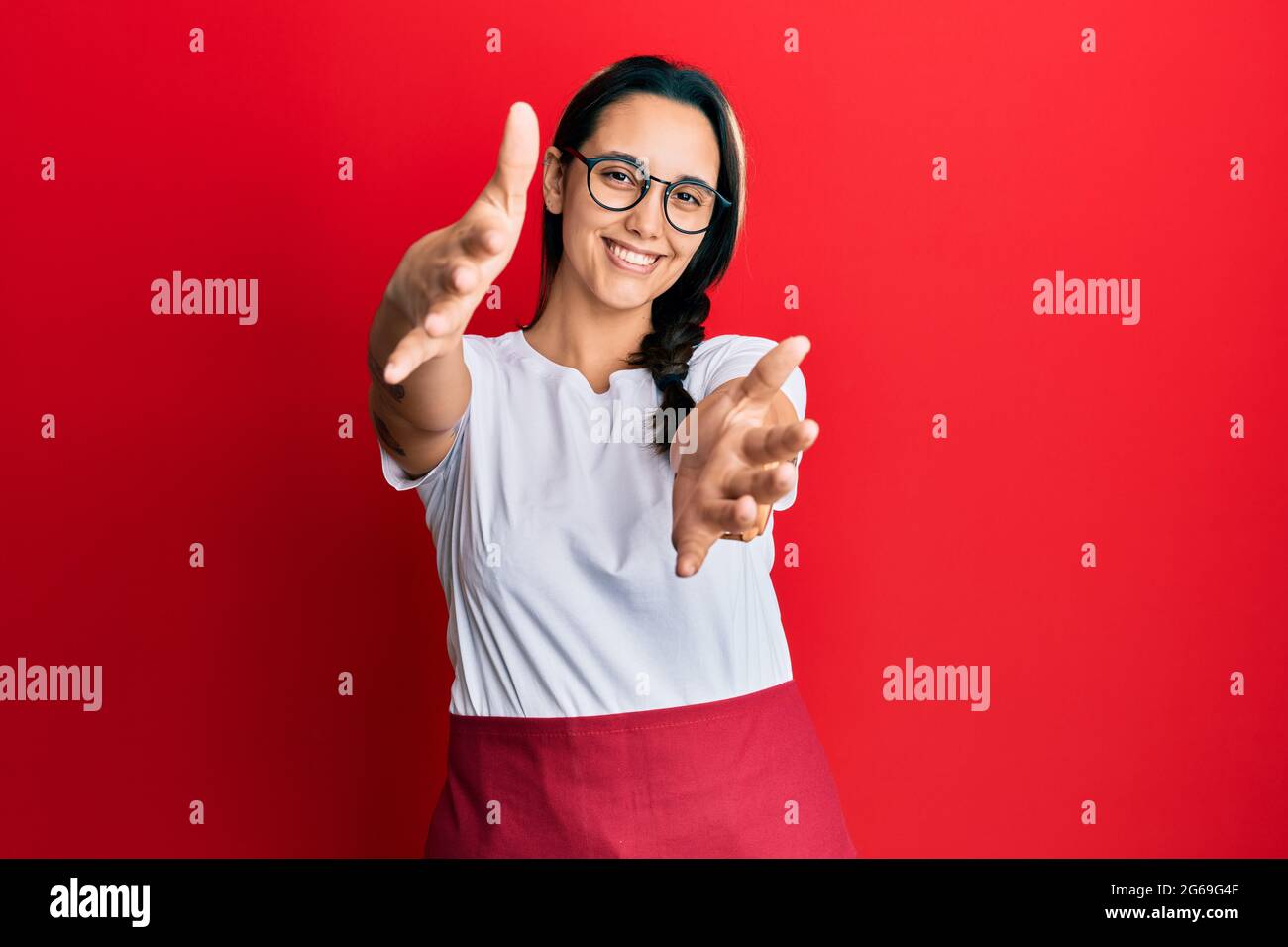 Young hispanic woman wearing professional waitress apron looking at the ...