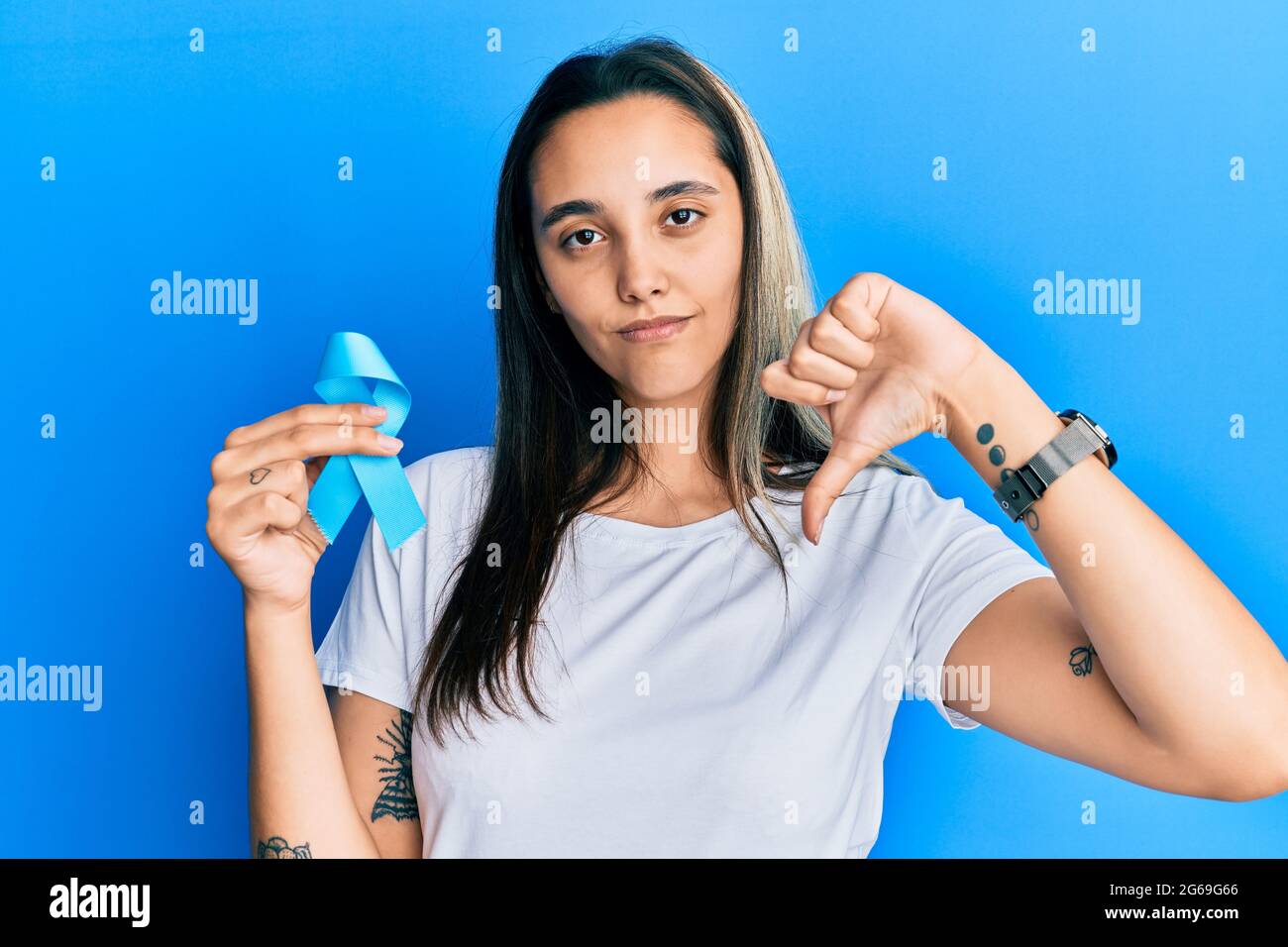Young hispanic woman holding blue ribbon with angry face, negative sign ...