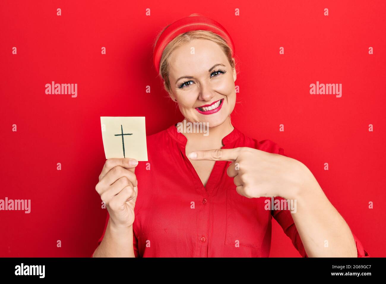 Young blonde woman holding catholic cross reminder smiling happy ...
