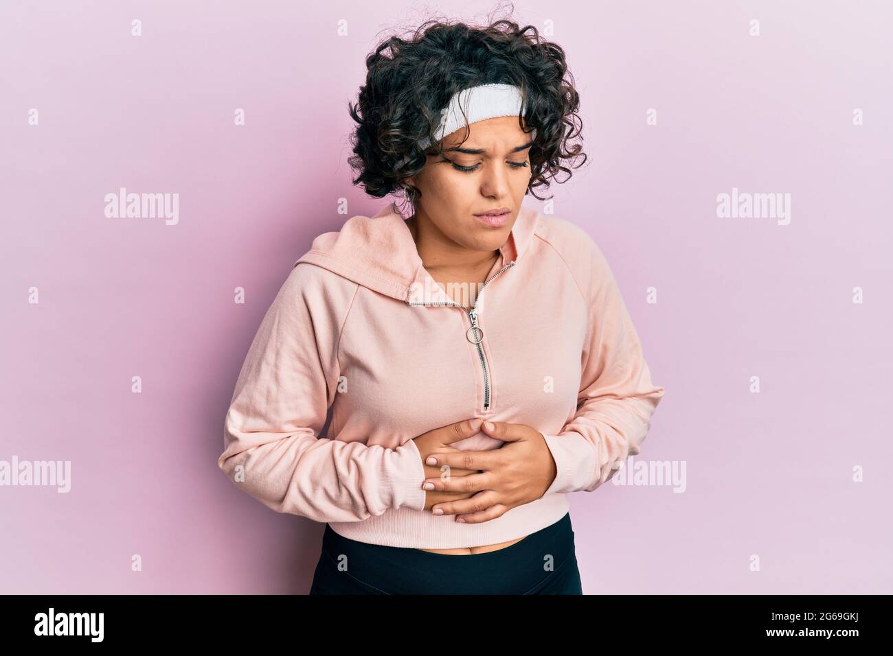 Young hispanic woman with curly hair wearing sportswear with hand on ...