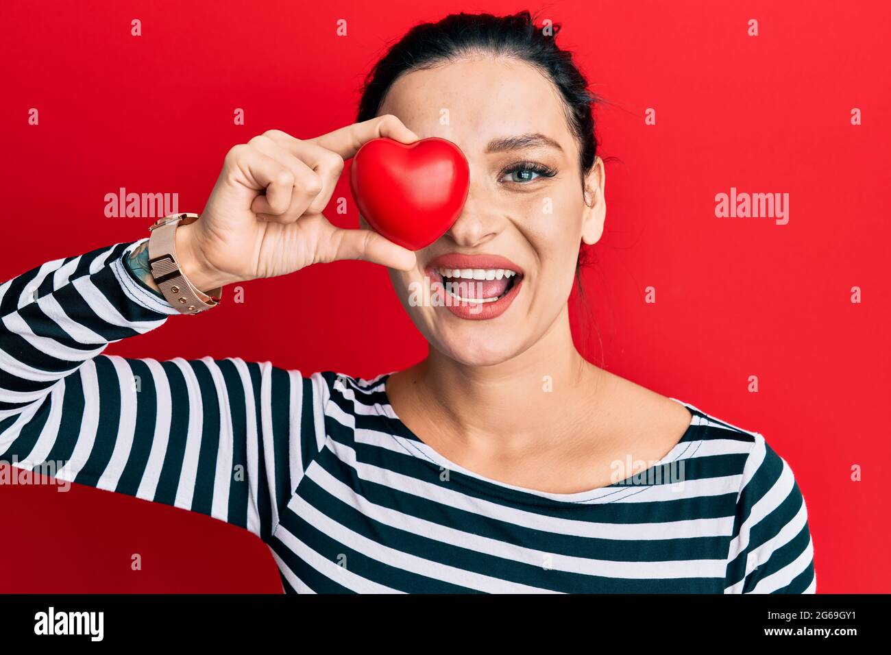 Young caucasian woman holding heart over eye looking positive and happy ...