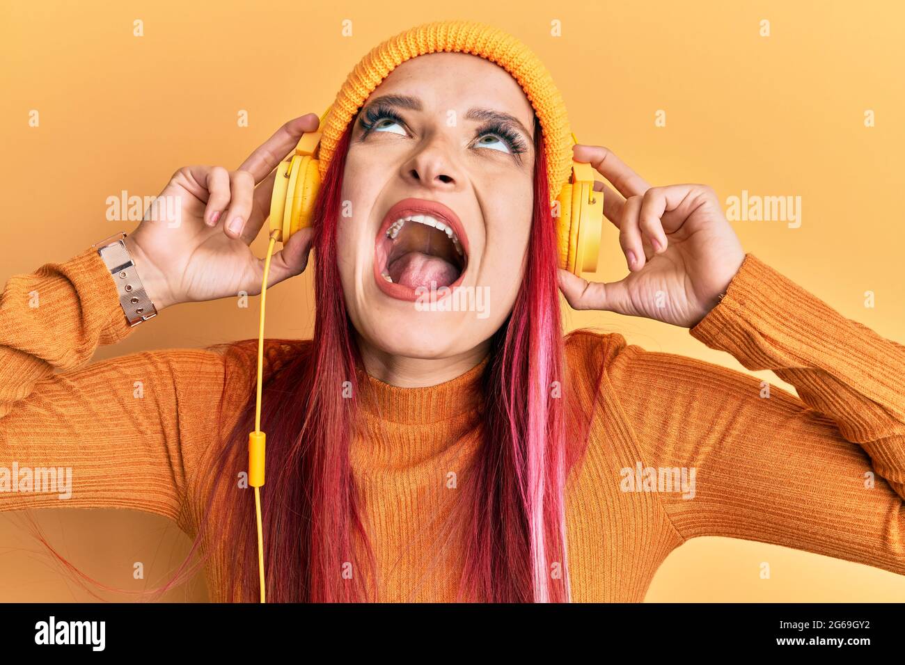 Young caucasian woman listening to music using headphones angry and mad ...