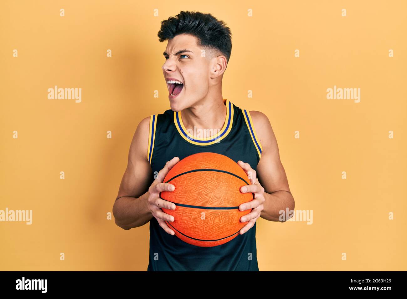 Young hispanic man holding basketball ball angry and mad screaming ...