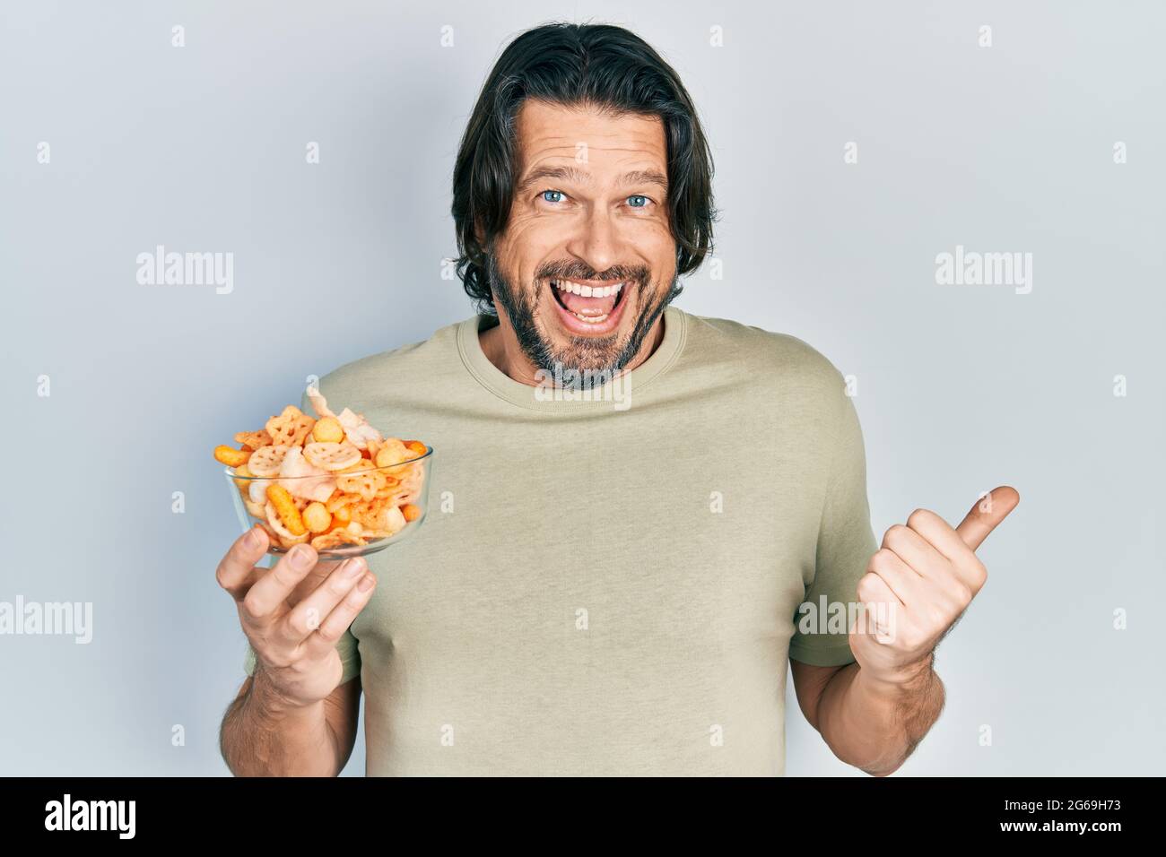 Middle age caucasian man holding potato chip pointing thumb up to the ...