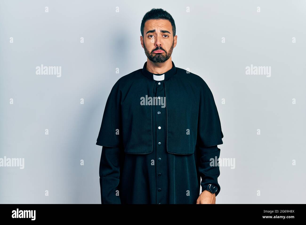 Handsome hispanic man with beard wearing catholic priest robe depressed ...