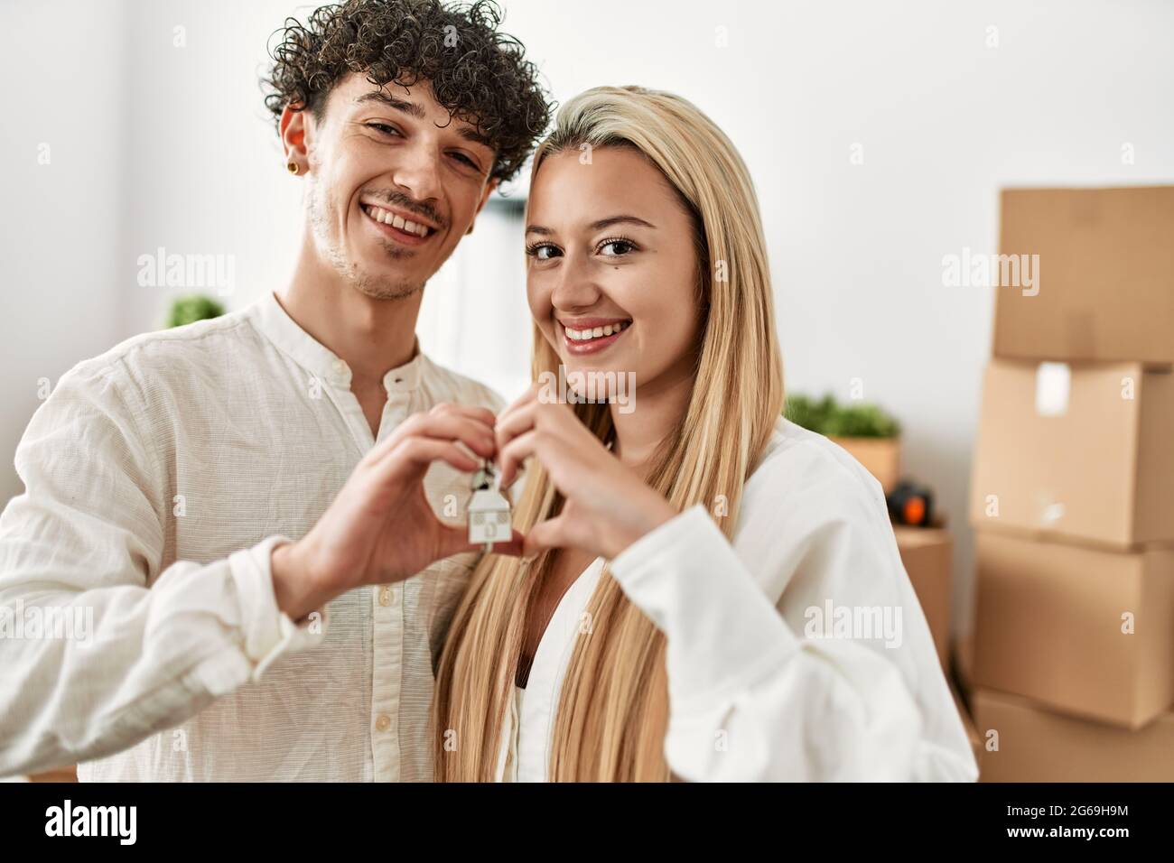 Young beautiful couple doing heart symbol with fingers and holding key ...