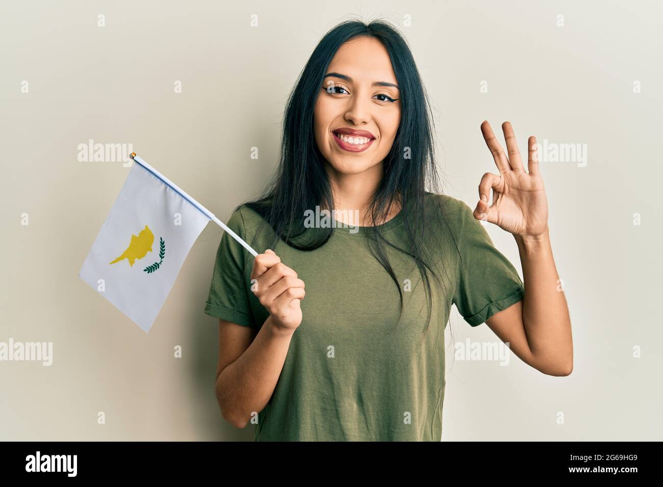 Young hispanic girl holding cyprus flag doing ok sign with fingers ...