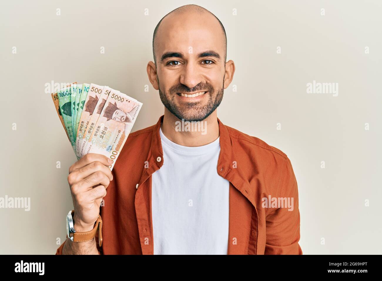 Young hispanic man holding south korean won banknotes looking positive ...