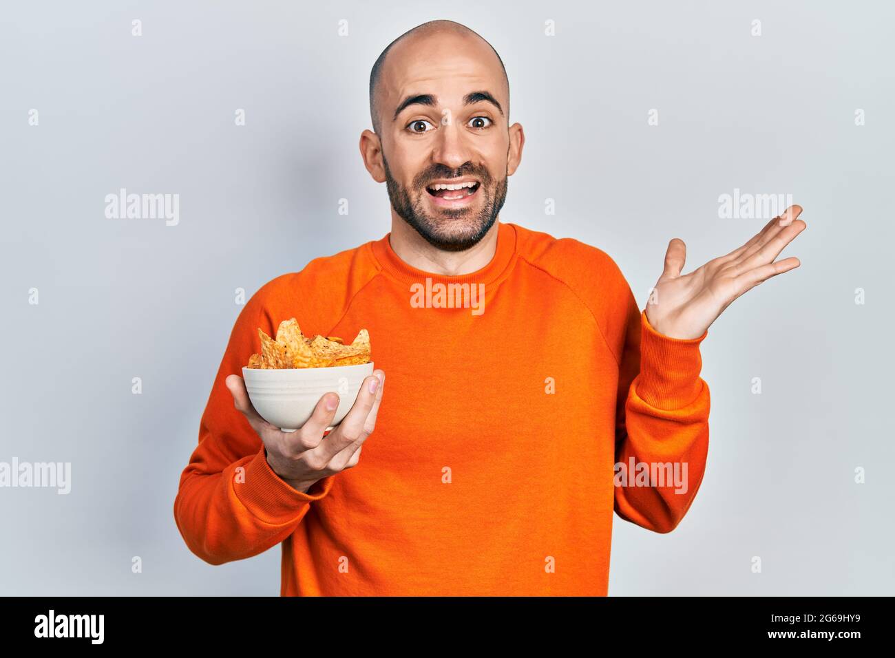 Young bald man holding nachos potato chips celebrating achievement with ...