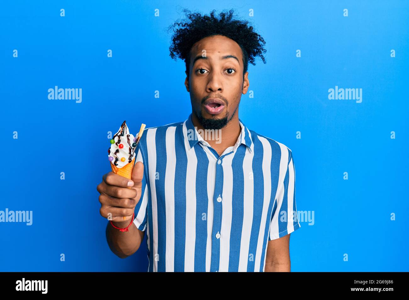 Young african american man with beard eating ice cream scared and ...
