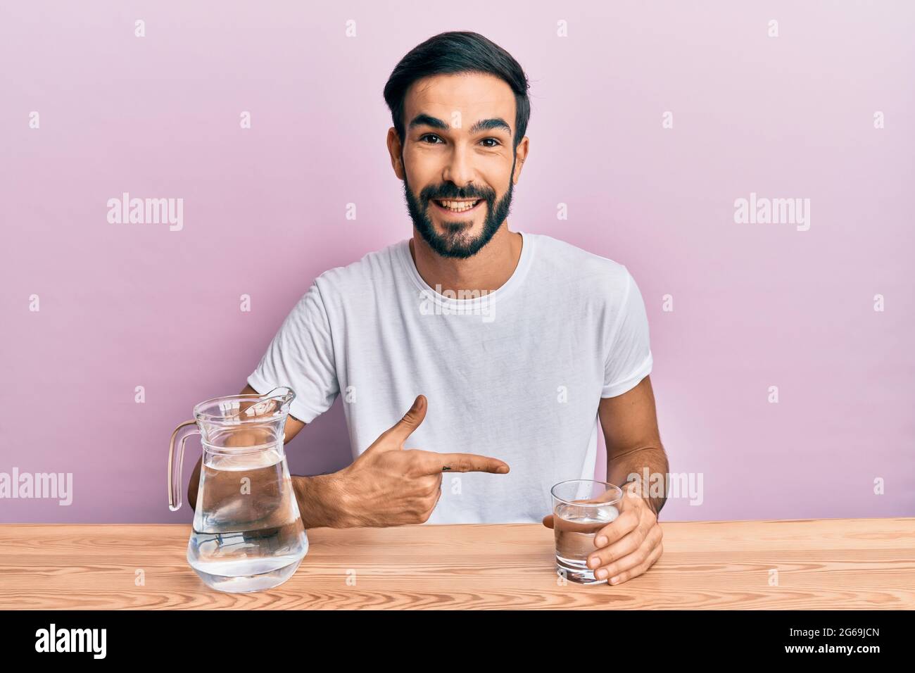 Young hispanic man drinking glass of water sitting on the table smiling ...