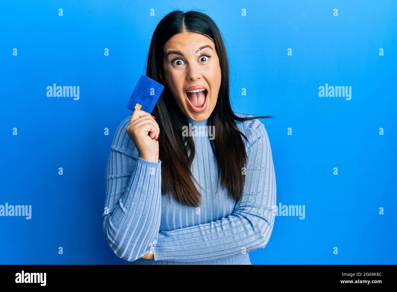 Beautiful brunette woman holding credit card celebrating crazy and ...