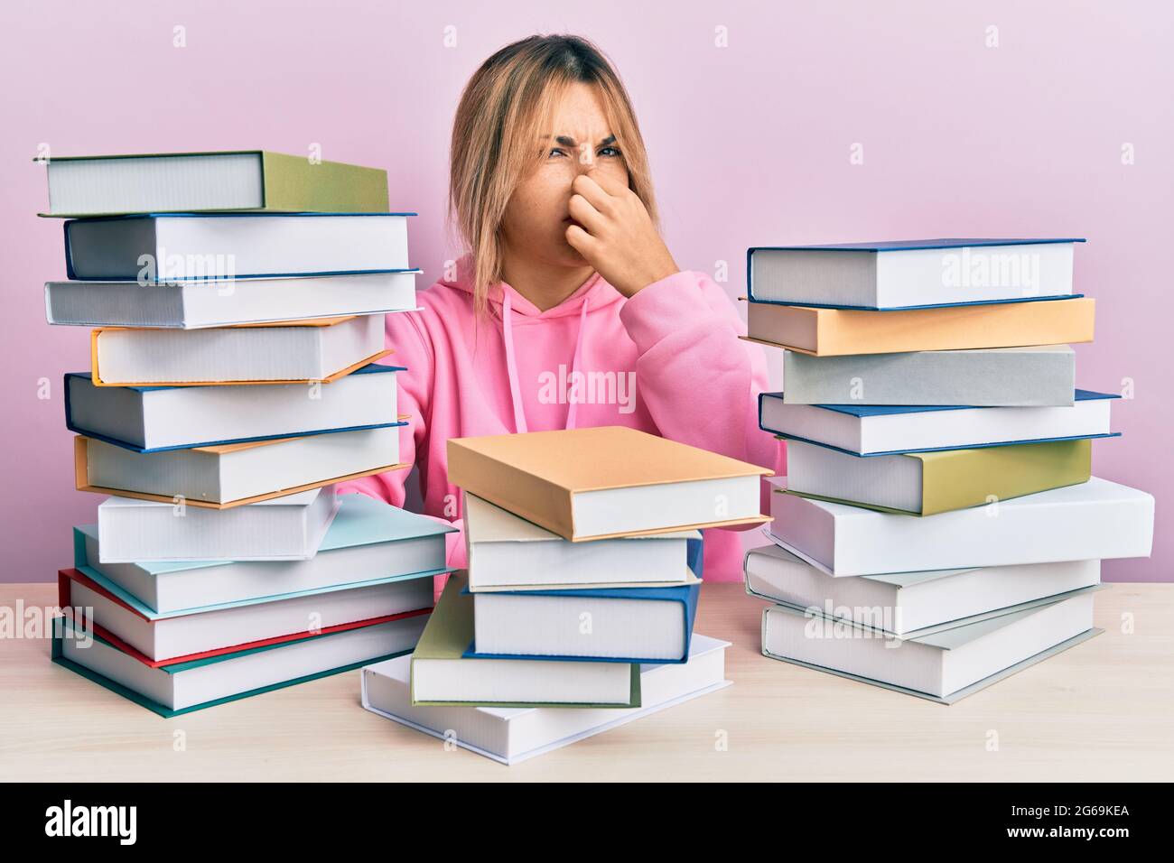 Young caucasian woman sitting on the table with books smelling ...