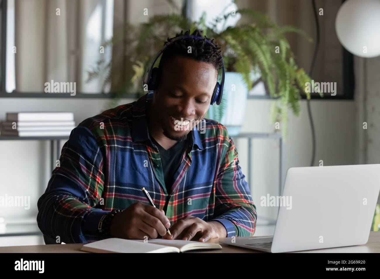 Smiling African American man in headphones taking notes, studying ...