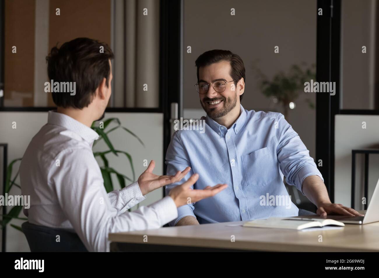 Two happy colleagues talking discussing project sitting at table Stock ...