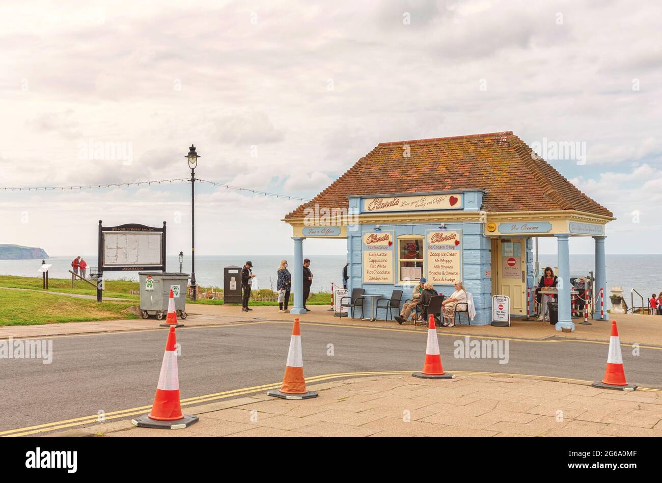 A small cafe on a cliff top. People queue outside and other sit at ...