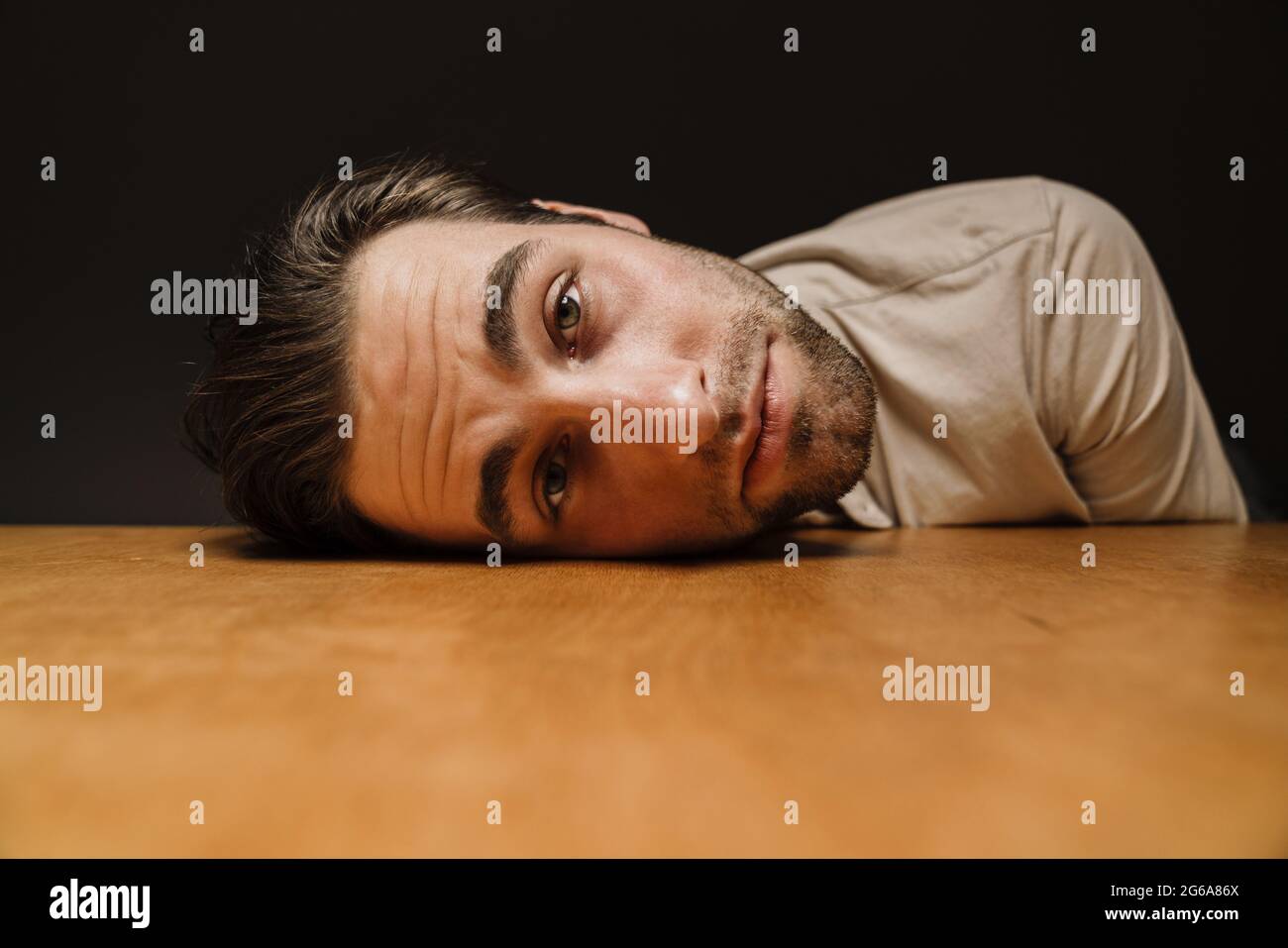 Upset sad man laying his head on a table indoors, looking at camera ...