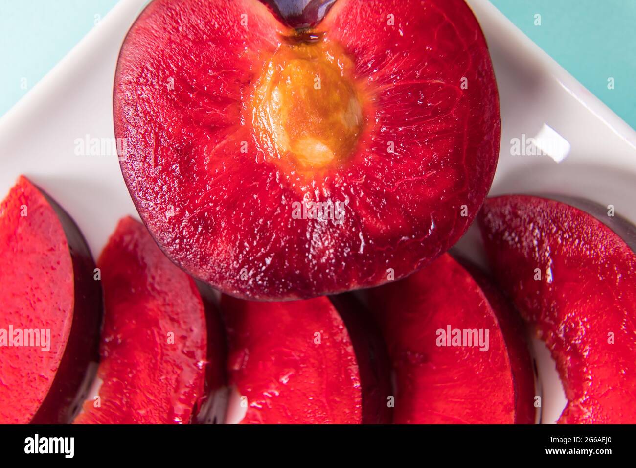 On a white saucer, a large plum, cut in half, with slices next to it ...