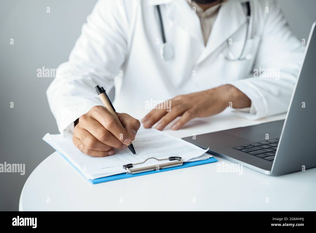 Mid-section arabian male doctor hands writing in patient checklist form ...