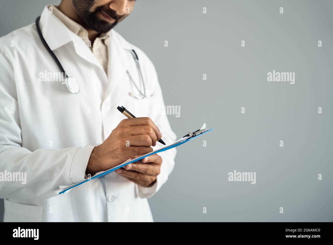 Mid-section of doctor write diagnosis in patient card against studio ...