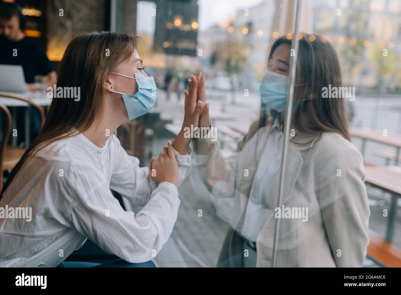 Two women in protective masks opposite each other, window between them ...