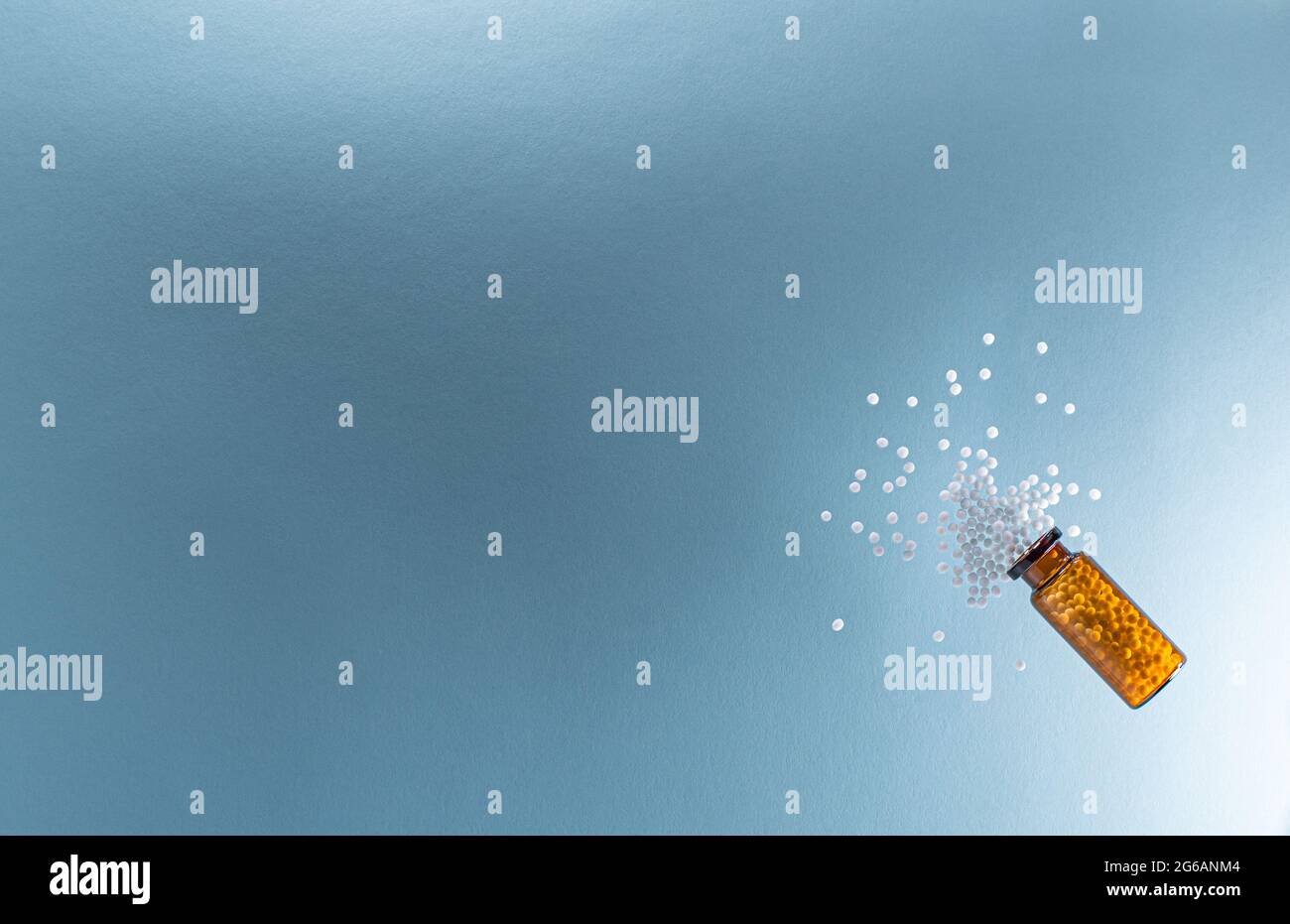 Homeopathic pellets are scattered from a glass jar on a blue surface ...