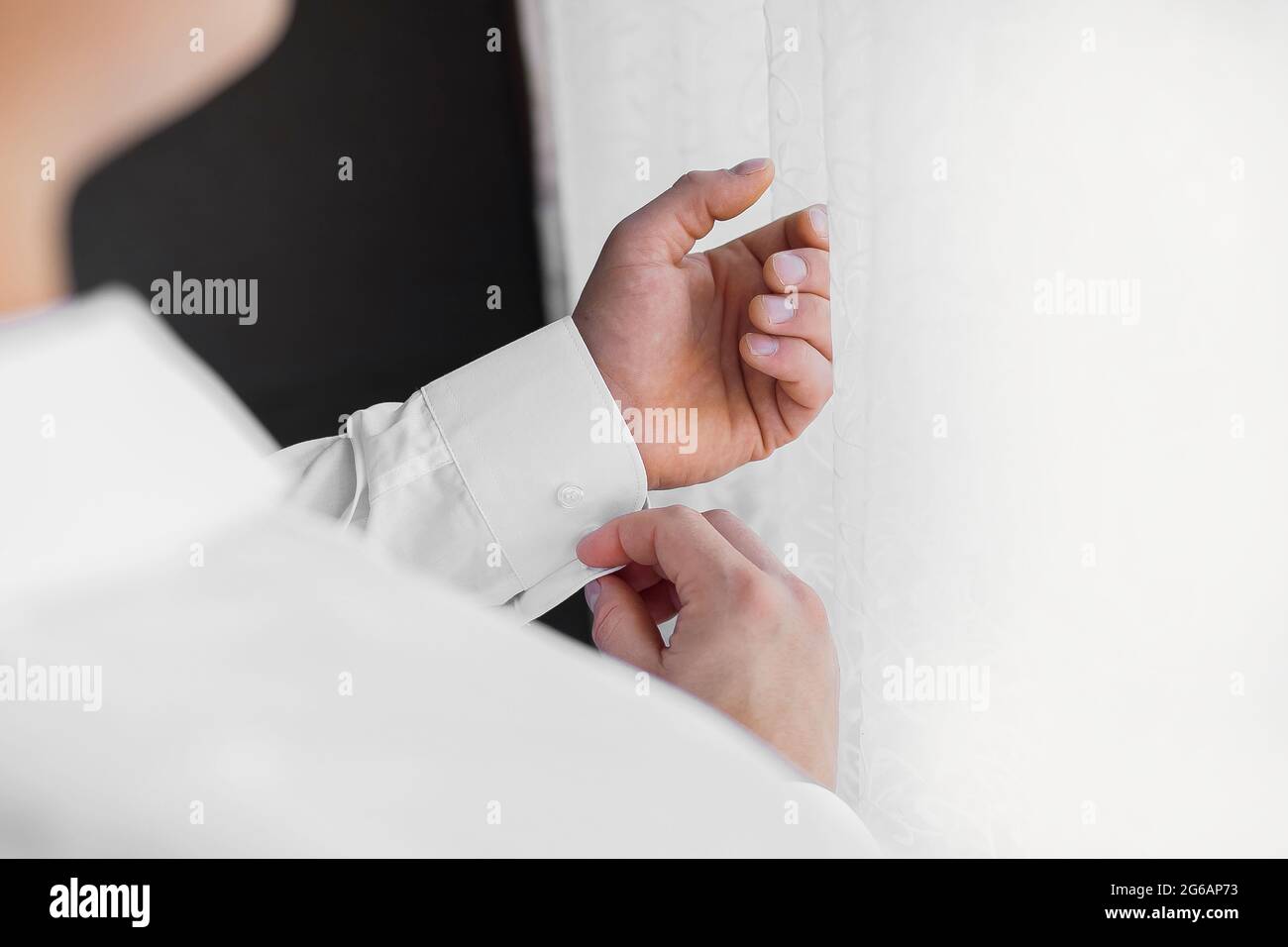 A man in a white shirt clasps his sleeves standing by the light from ...