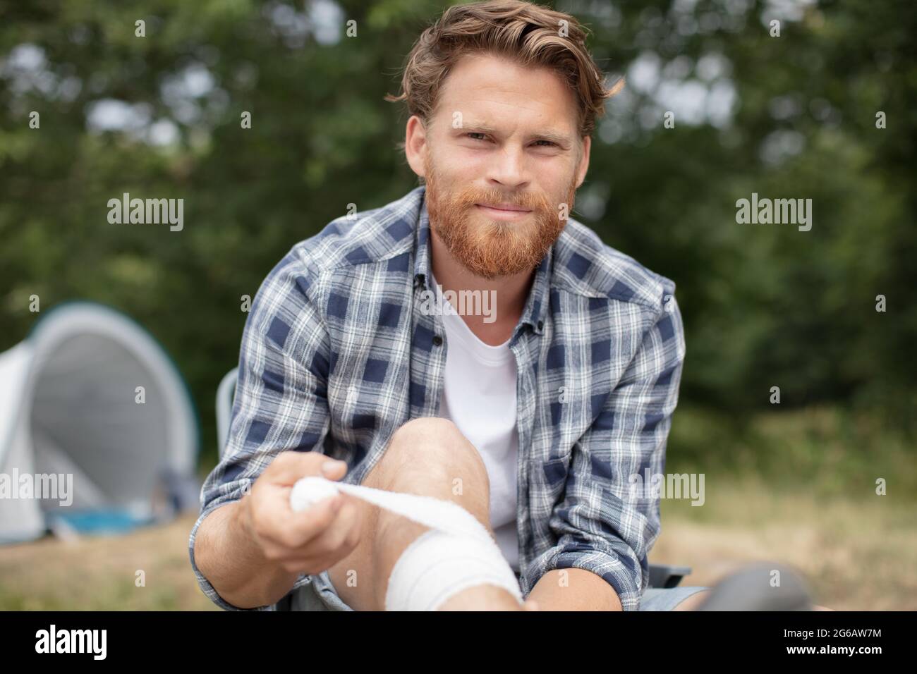 young man applying bandage while camping Stock Photo - Alamy