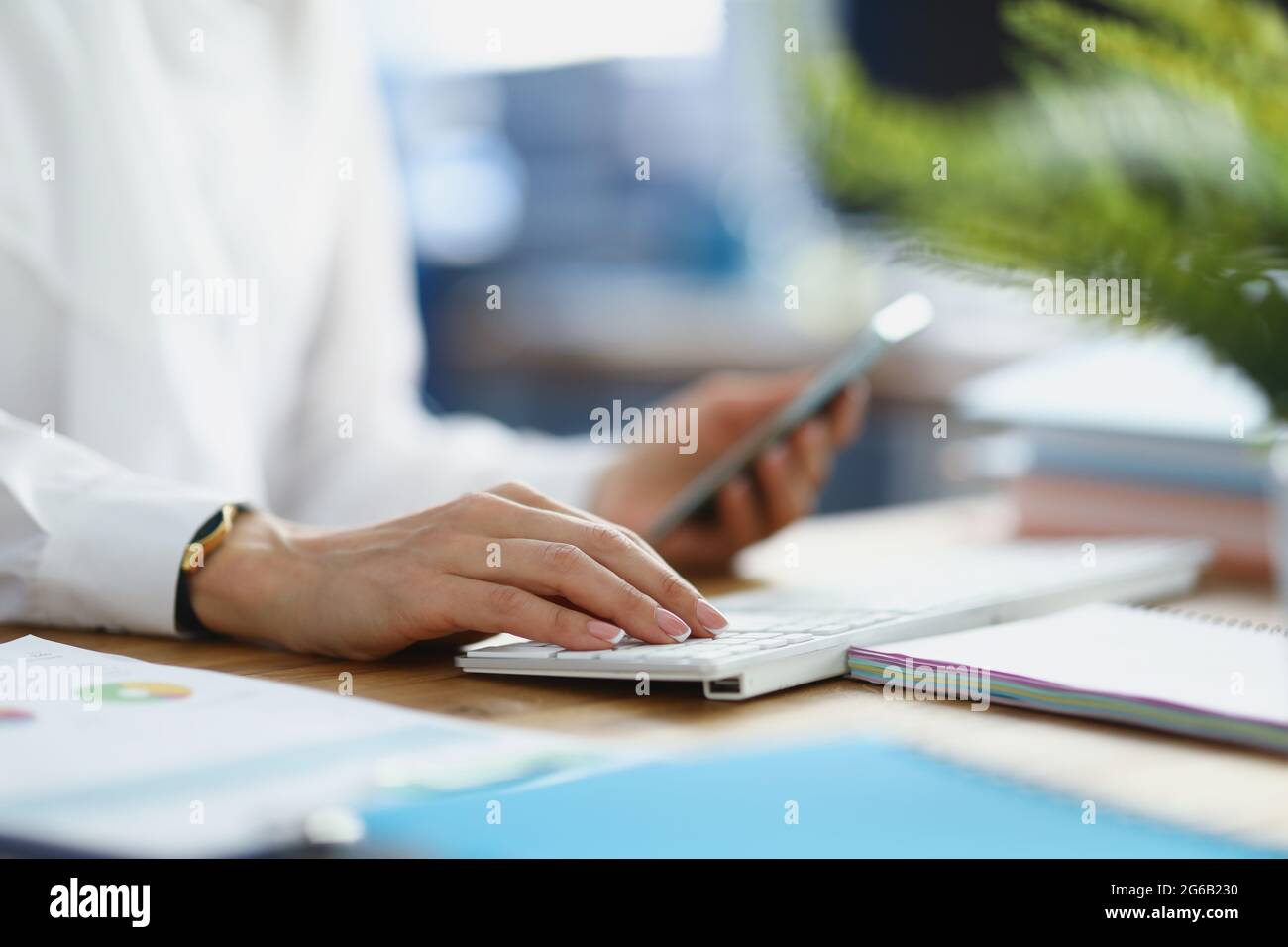 Woman holding mobile phone in hands and typing on laptop keyboard Stock ...