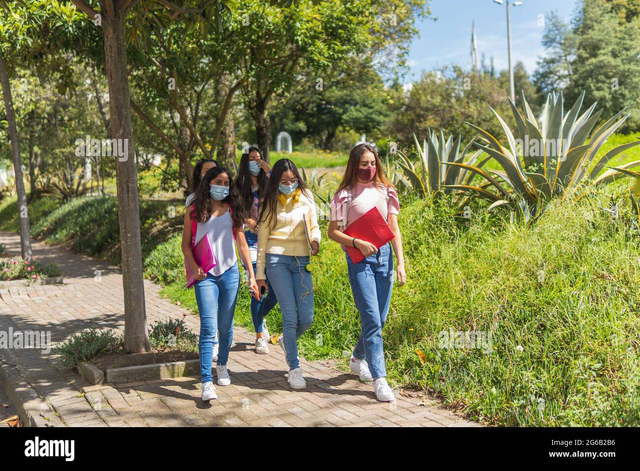 A group of Latina teenage friends walk to class wearing face masks as a ...