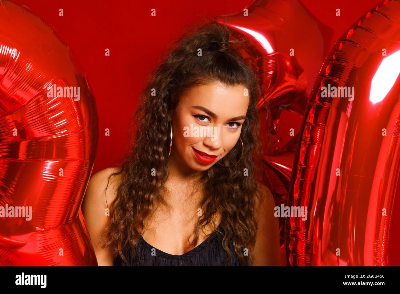 Portrait of happy 30 year old woman on red background with red balloons ...