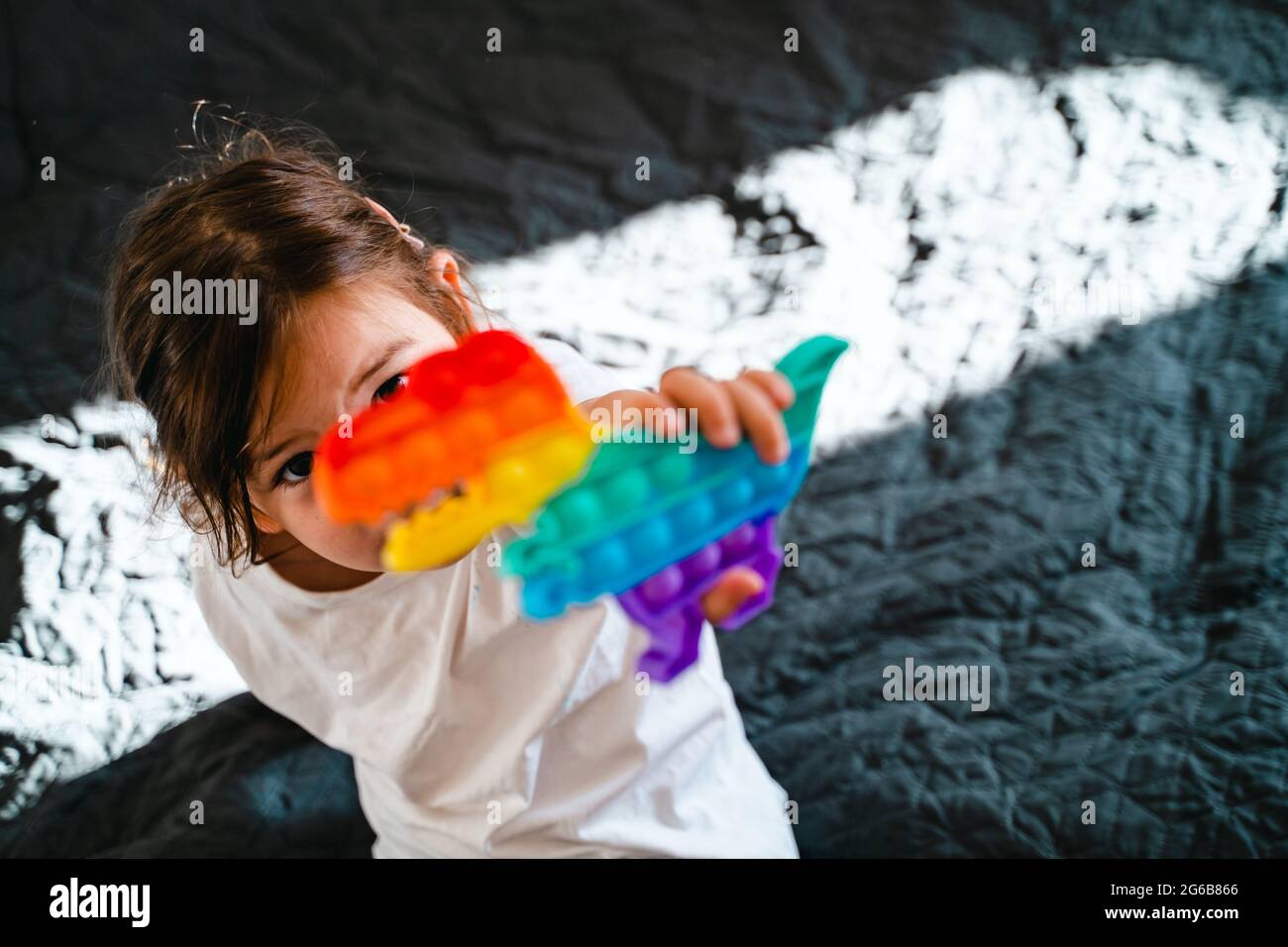 Toddler girl with popit toy in rainbow colours. Dino shape silicone toy ...