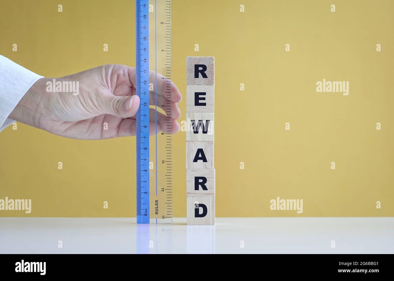 Woman's hand using ruler to measure reward. On yellow background, copy ...