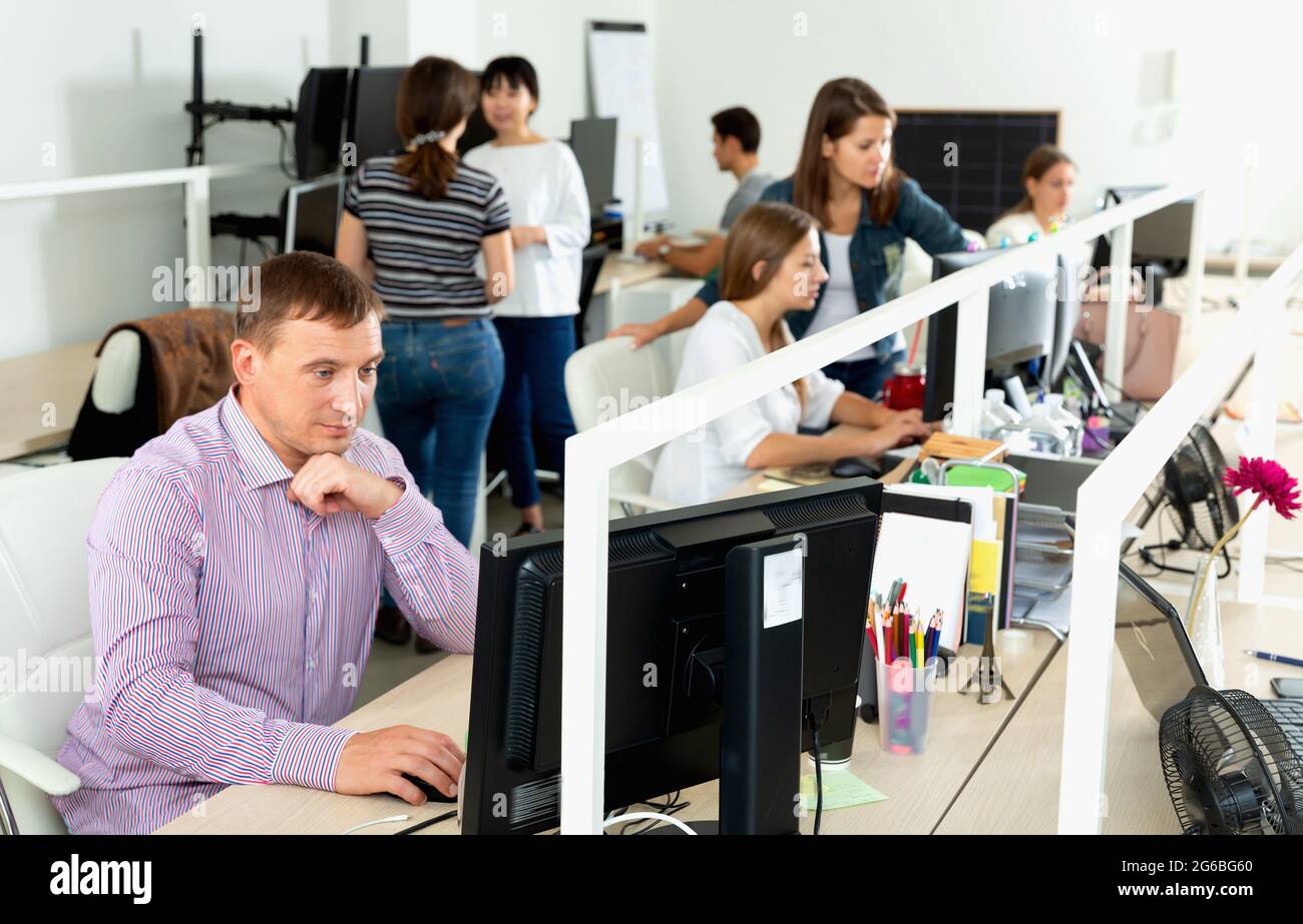 Handsome young man confidently working on computer in modern open plan ...