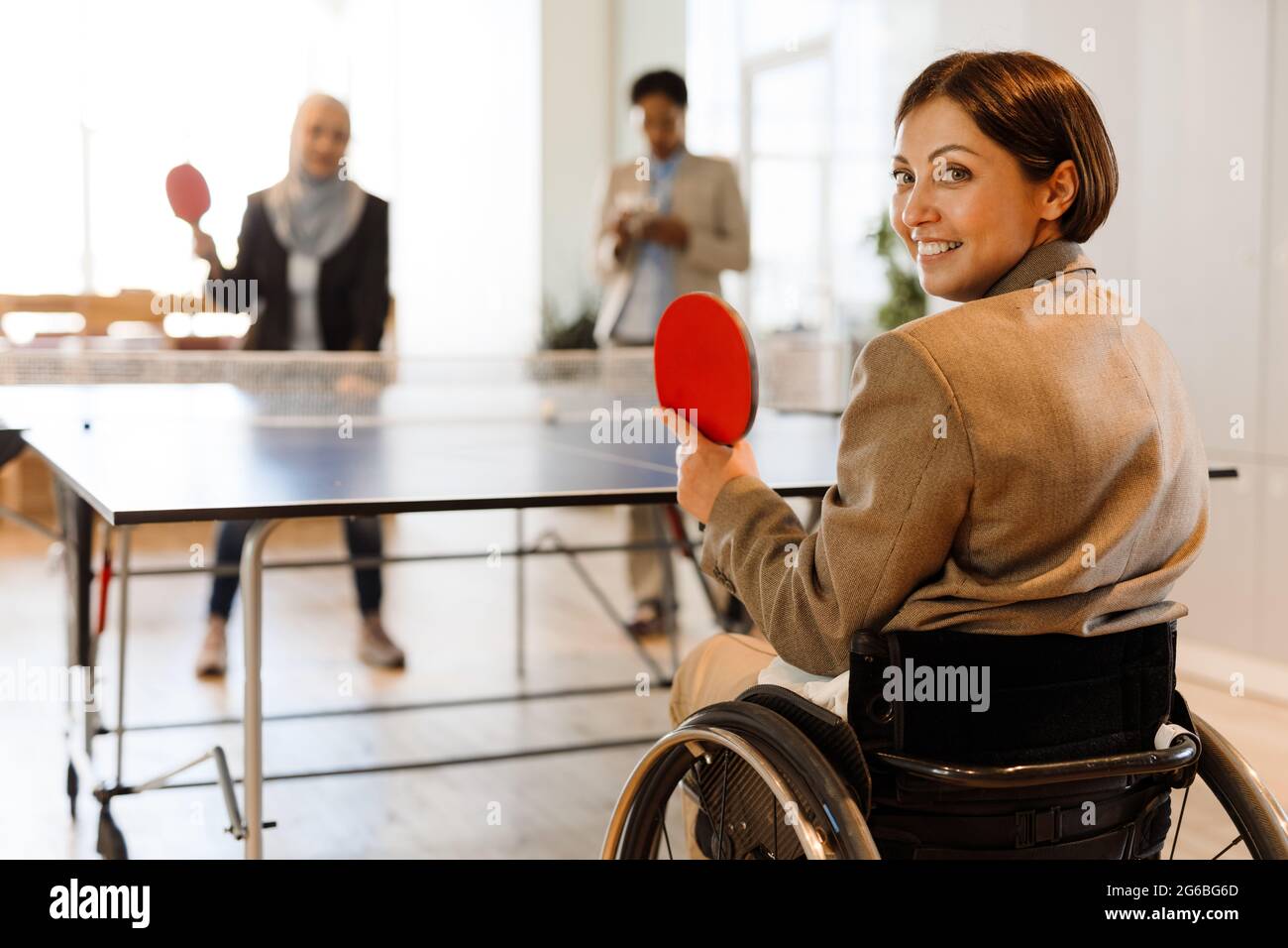 White woman in wheelchair playing ping-pong with her colleague at ...