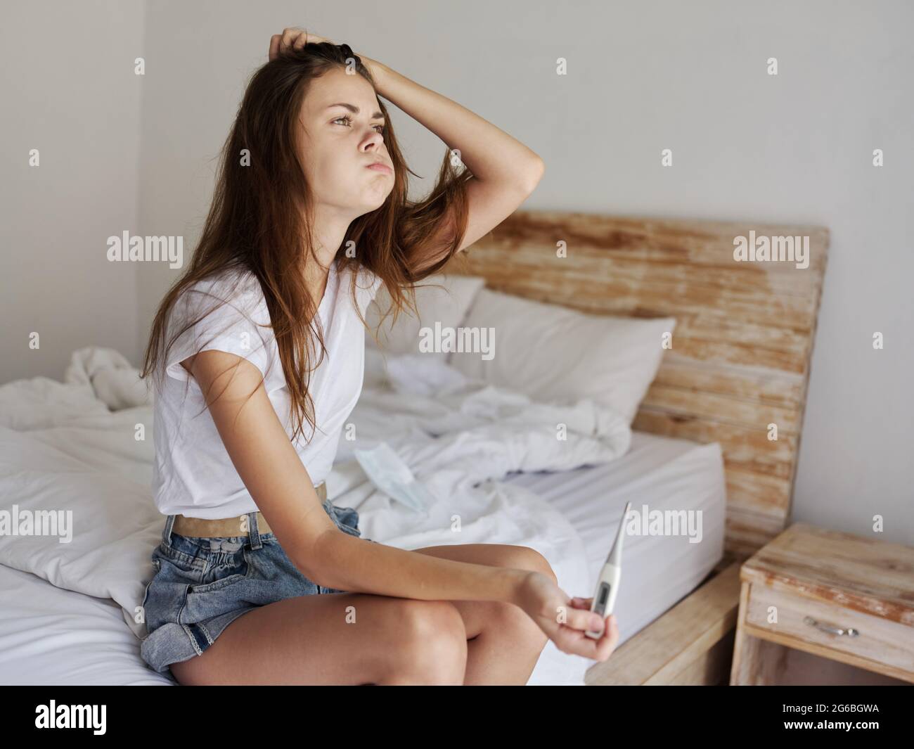 a woman sits on a bed with a thermometer in her hands puffed out cheeks ...