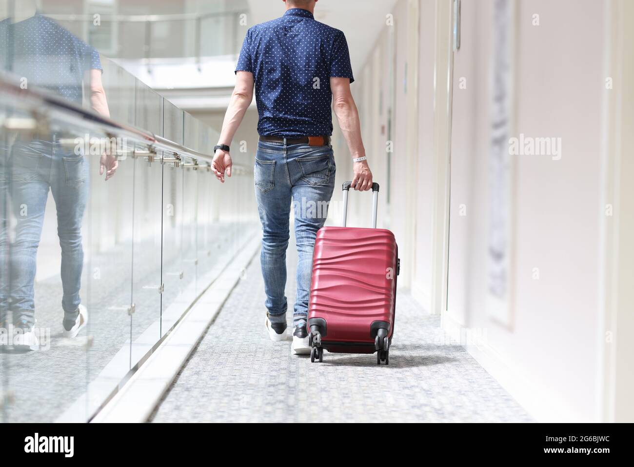 Rear view of man pulling suitcase down hotel corridor Stock Photo - Alamy