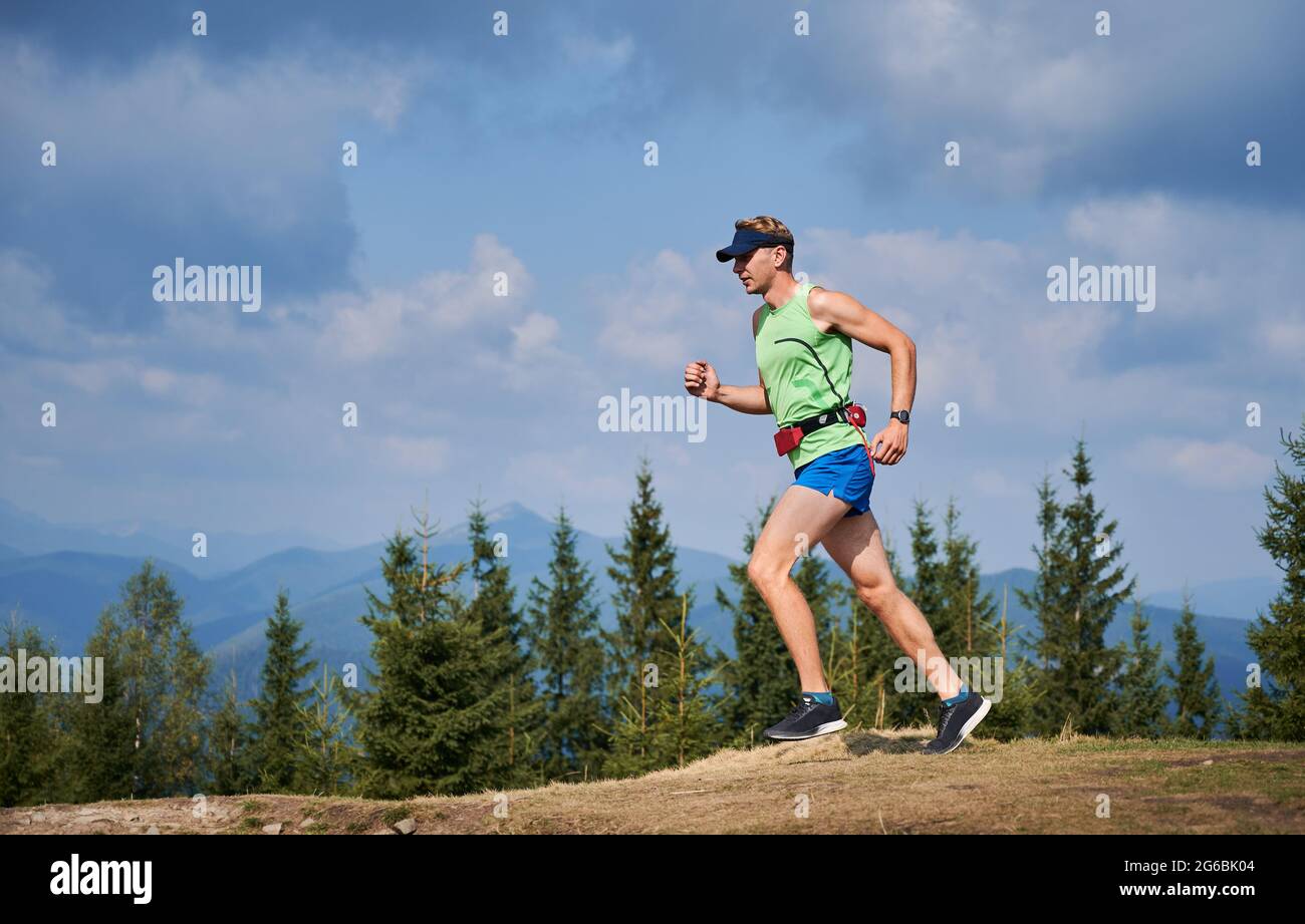 Side view of guy running in fresh air by mountain trails. Summer trail ...