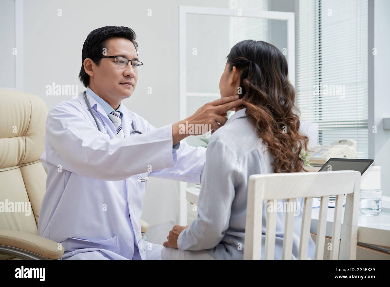 General practitioner touching neck of senior patient when checking her ...