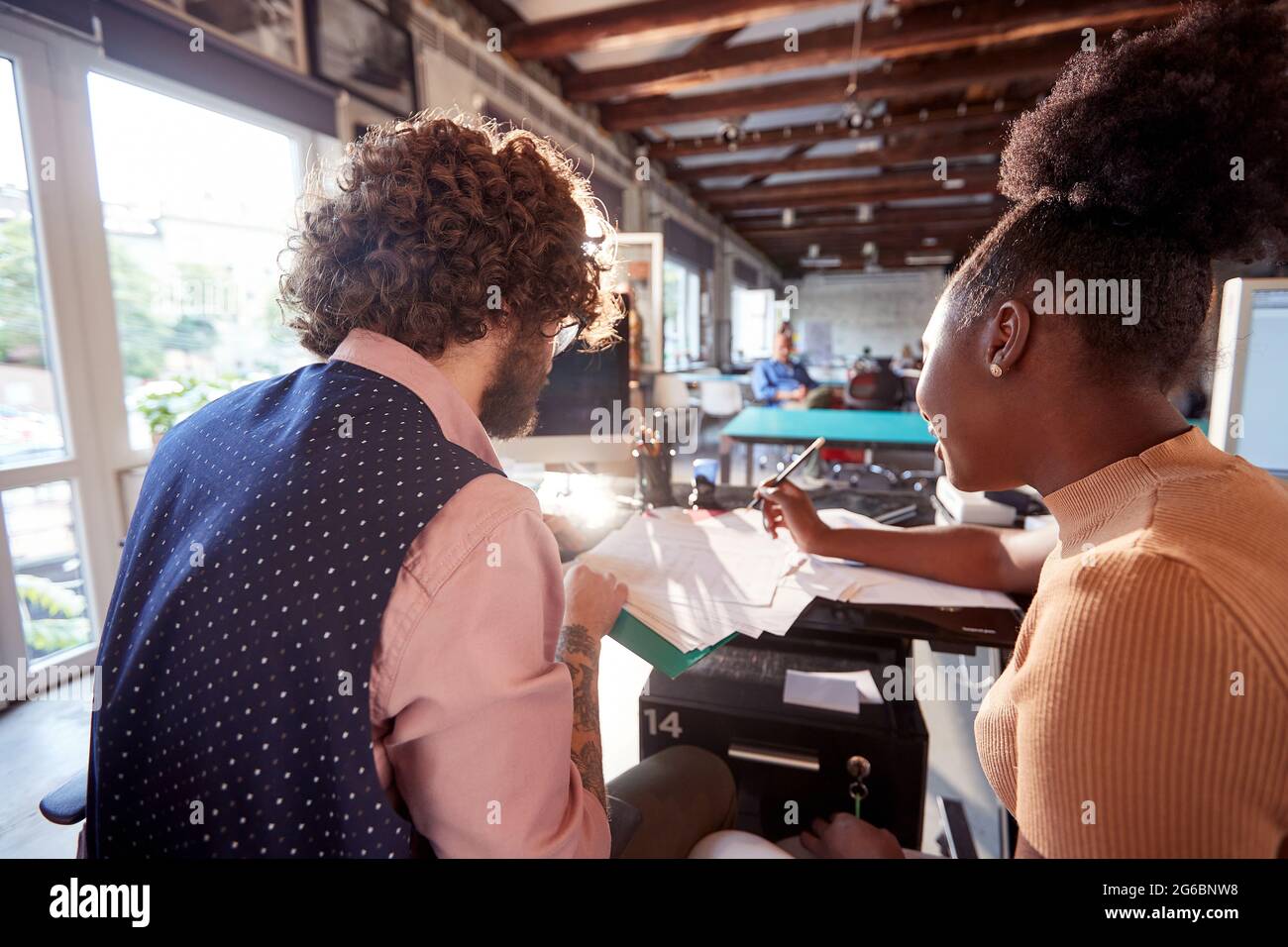 Two of young colleagues are passing through some documents at work in a ...