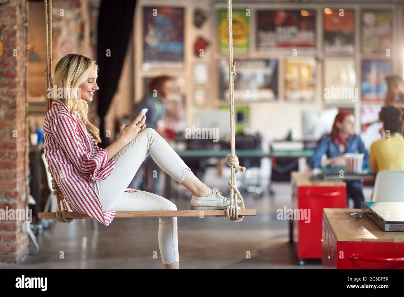 A young woman is texting on a smartphone while relaxing on a swing ...