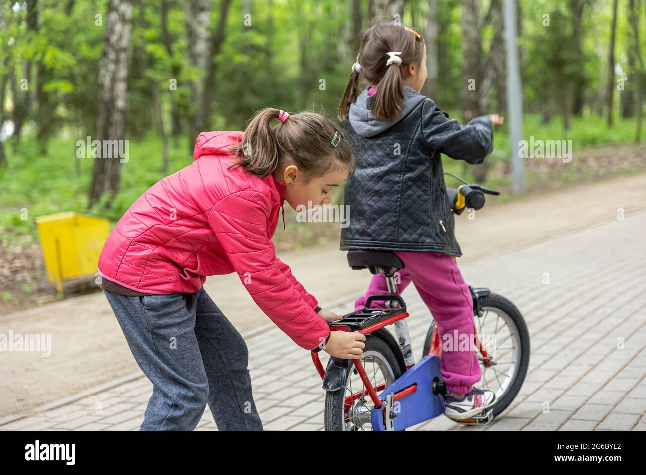Two little girls ride a bike in the park in spring Stock Photo - Alamy